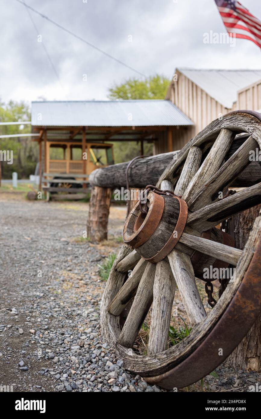 A rusted wheel is sitting on the ground next to a building. Scene is ...