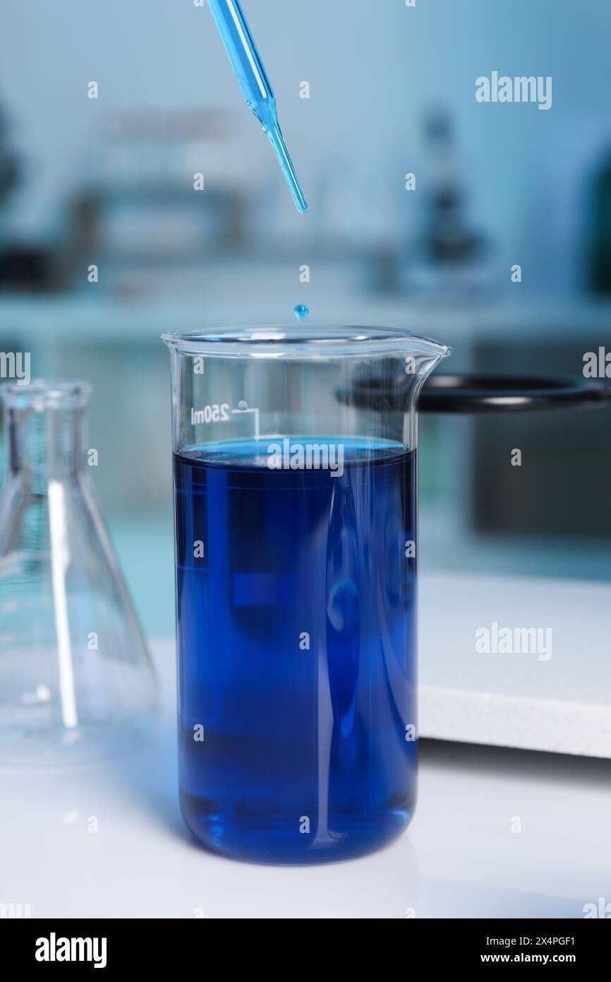 Laboratory analysis. Dripping blue liquid into beaker on white table ...