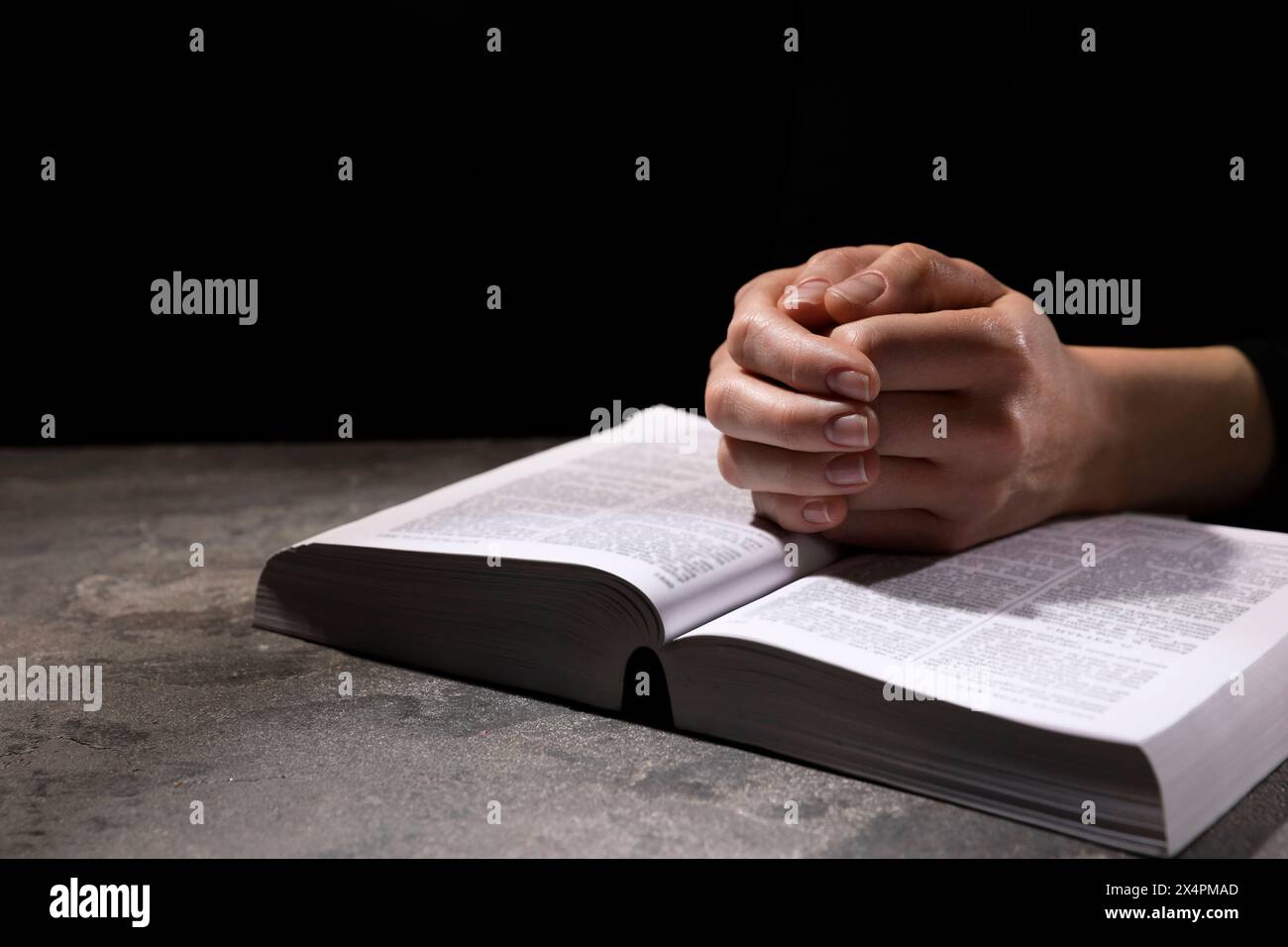 Religion. Christian woman praying over Bible at table against black ...
