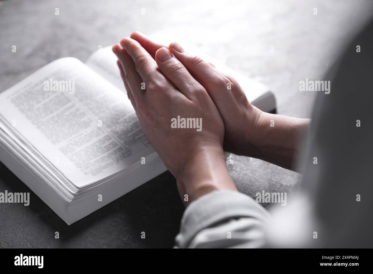Religion. Christian woman praying over Bible at gray table, closeup ...