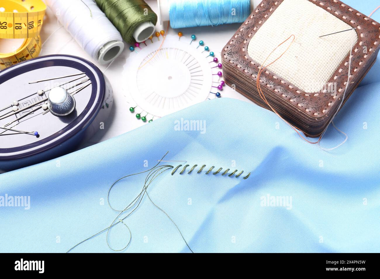 Light blue cloth with needle, thread and stitches near sewing tools on ...