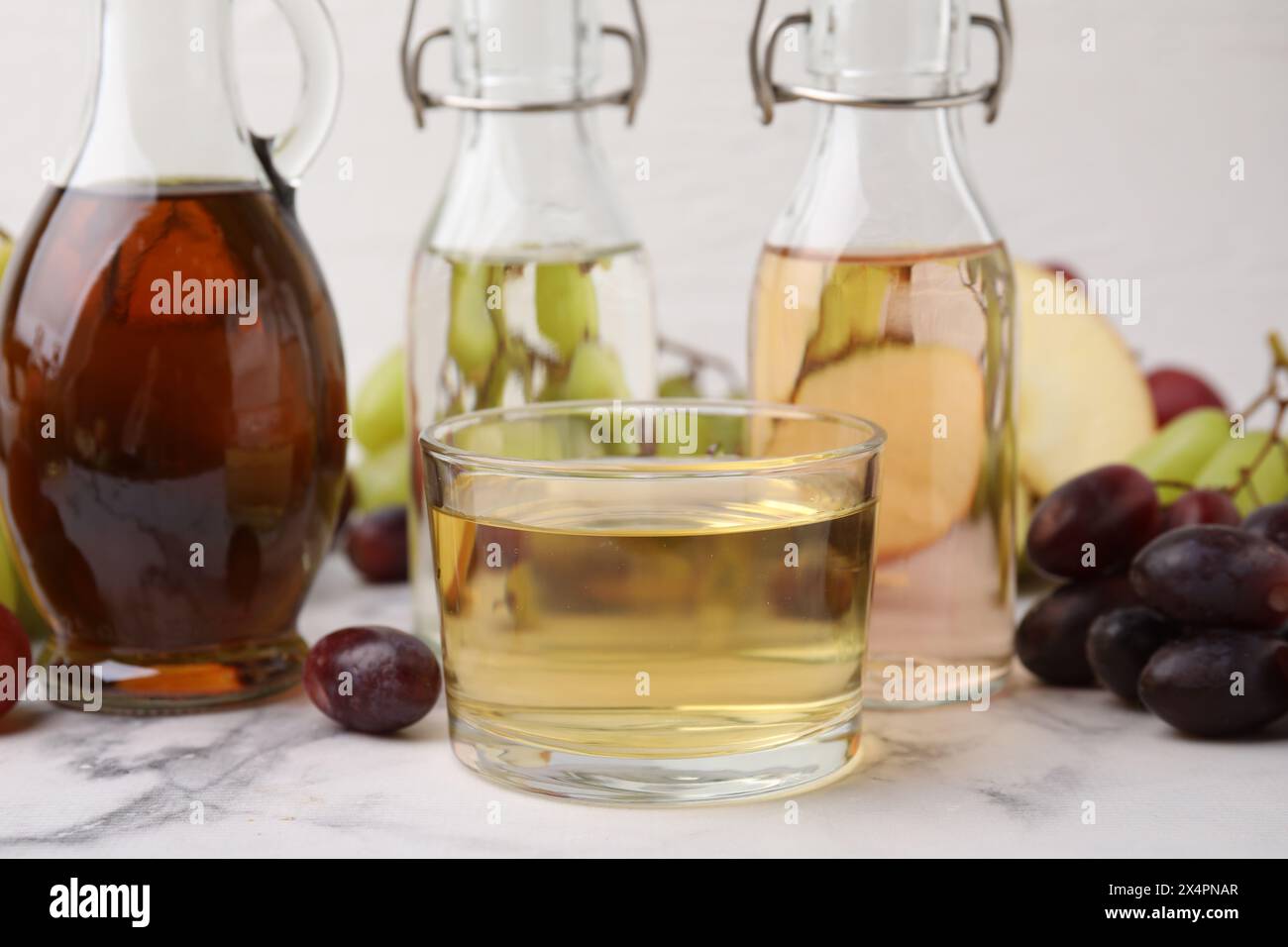Different types of vinegar and grapes on light marble table, closeup ...