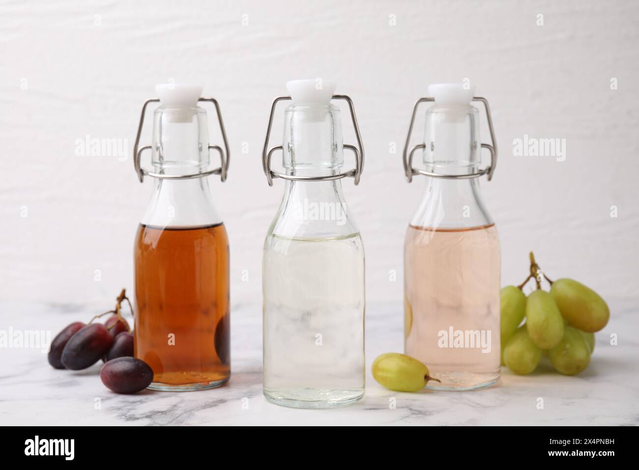 Different types of vinegar in bottles and grapes on light marble table ...