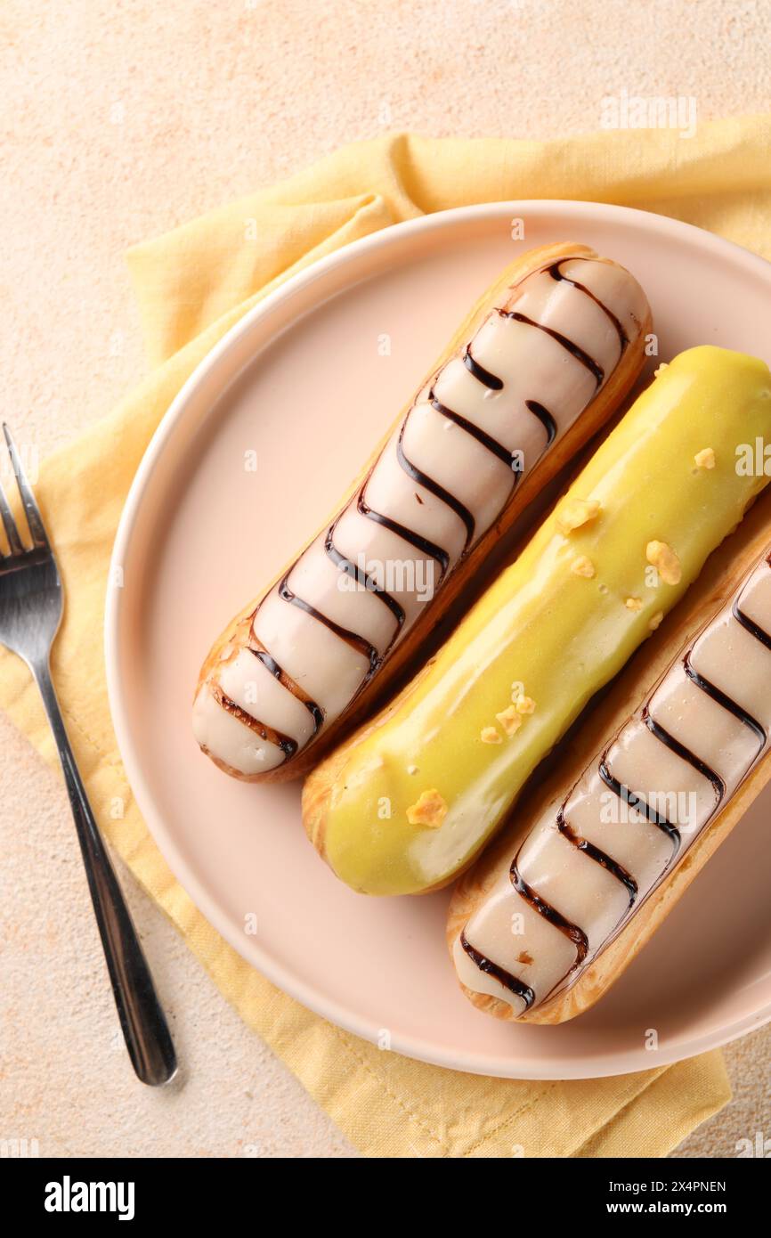 Different tasty glazed eclairs served on color textured table, top view ...
