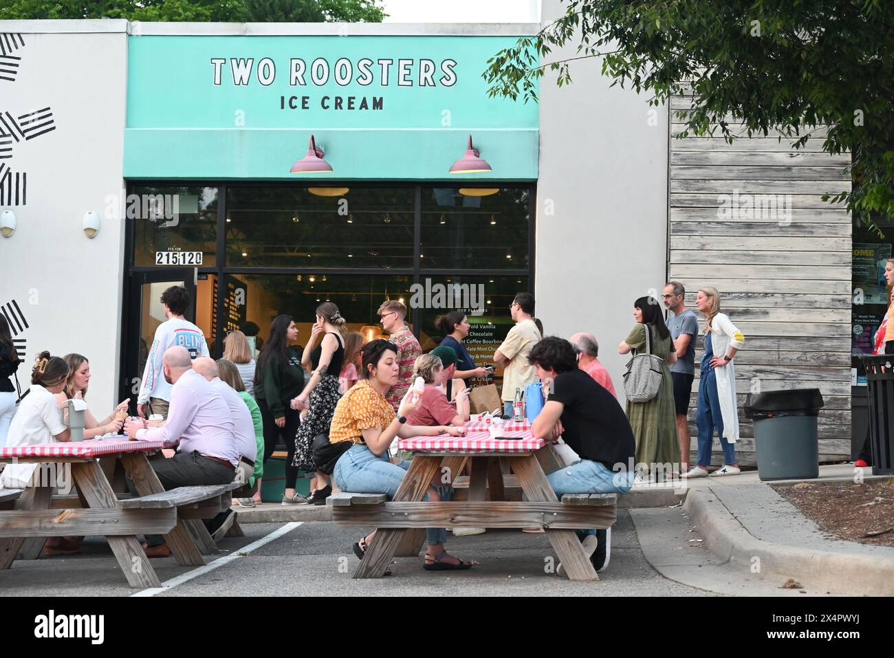 Customers enjoy ice cream on picnic tables outside while a line of ...
