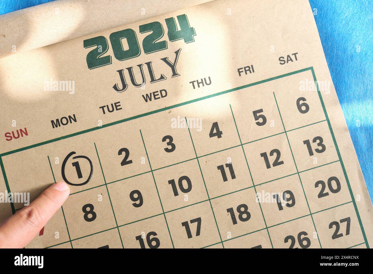 Hand pointing on July 1 2024 date on calendar flat lay in blue ...