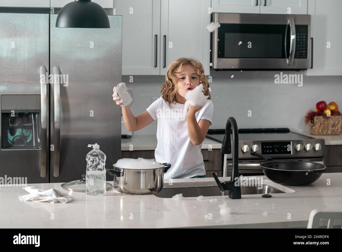 Home chores. Kid in kitchen cleaning plates. Cute boy washing dishes in ...