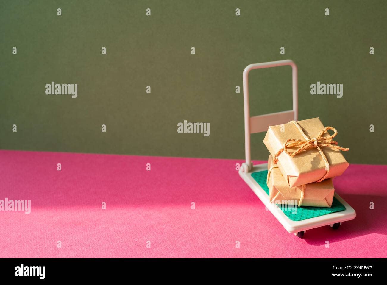 Trolley cart with gift boxes on pink and khaki green background. Parcel ...