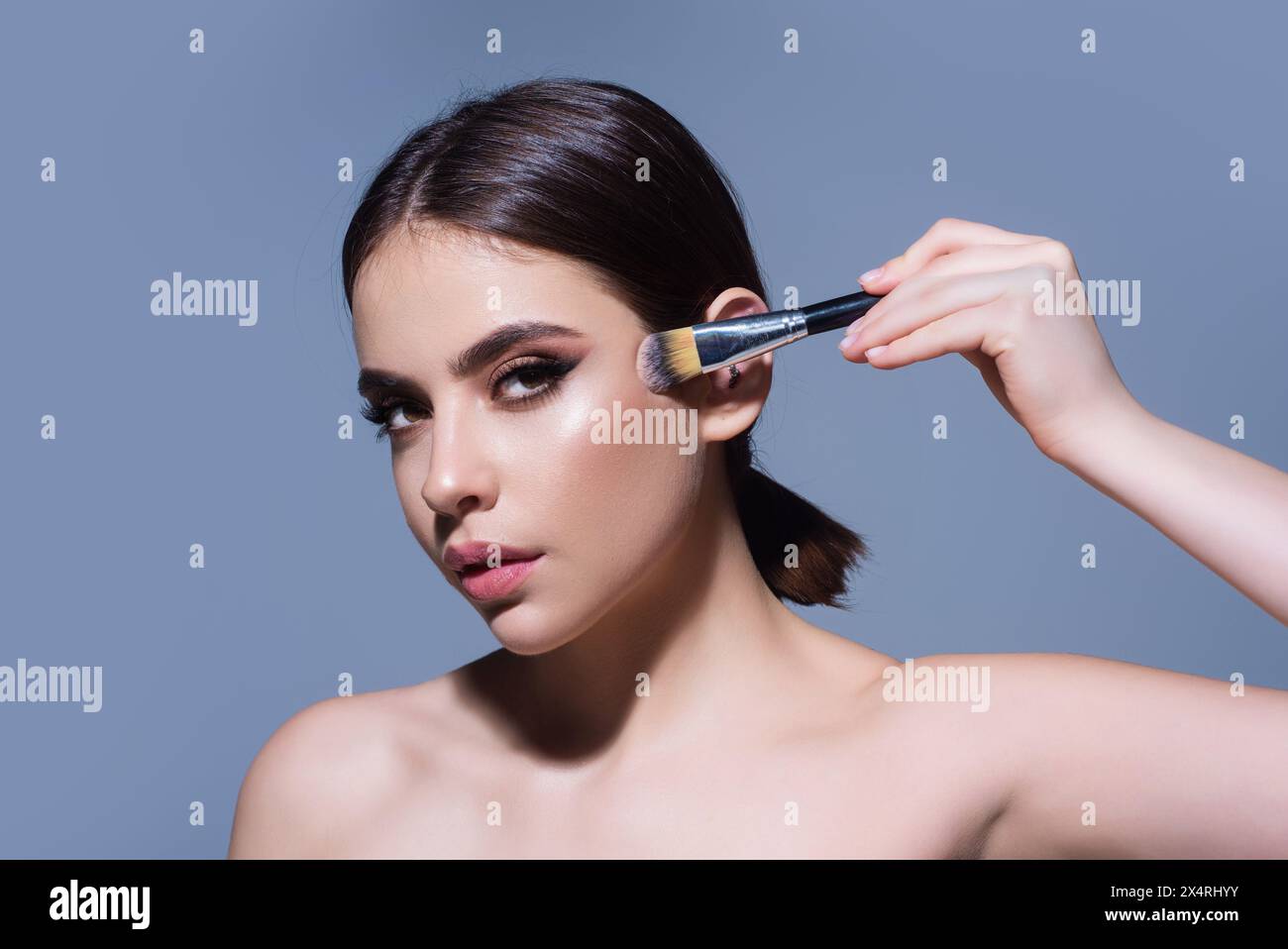 Studio portrait of a woman applying cosmetic tonal foundation on face ...