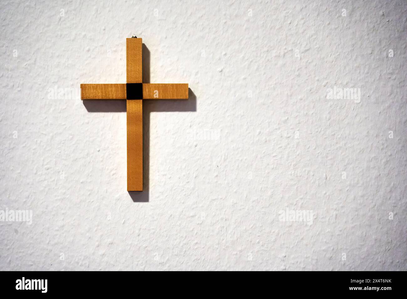 Simple wooden cross casting a shadow on a textured white wall, symbolizing faith and ...