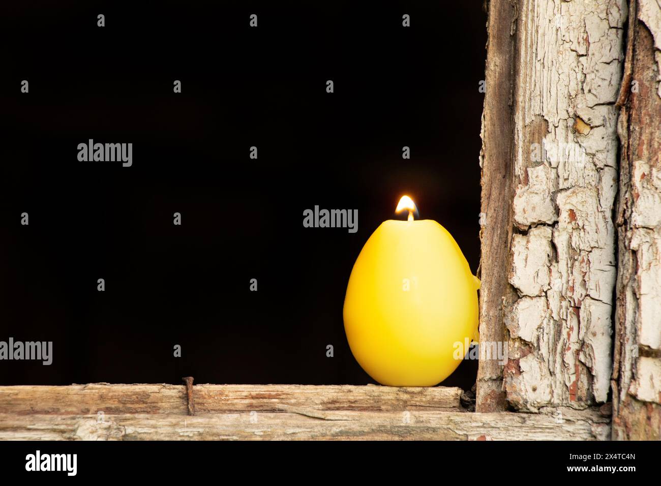A burning candle in the shape of a yellow chicken egg stands on a ...