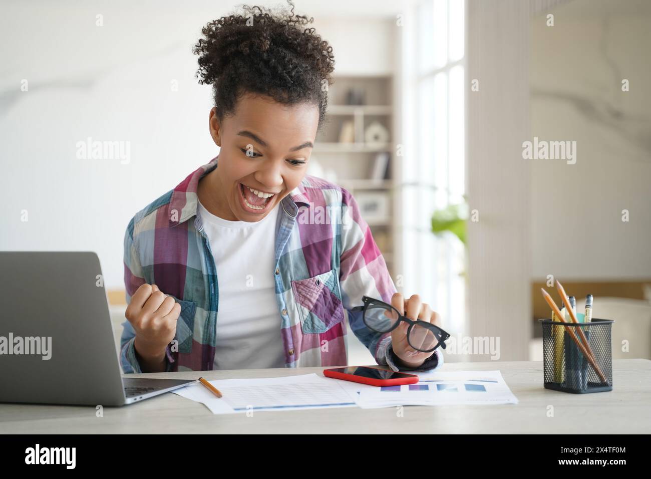 Exhilarated young woman celebrates triumphantly in front of her laptop ...