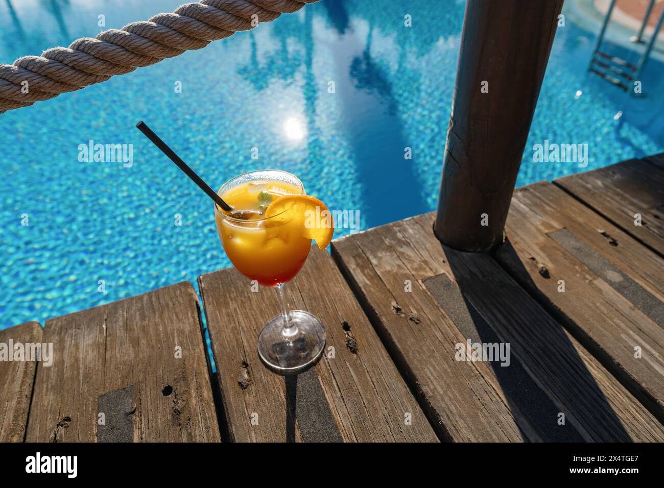 Tropical cocktail on a wooden deck by a pool, featuring a blue water ...