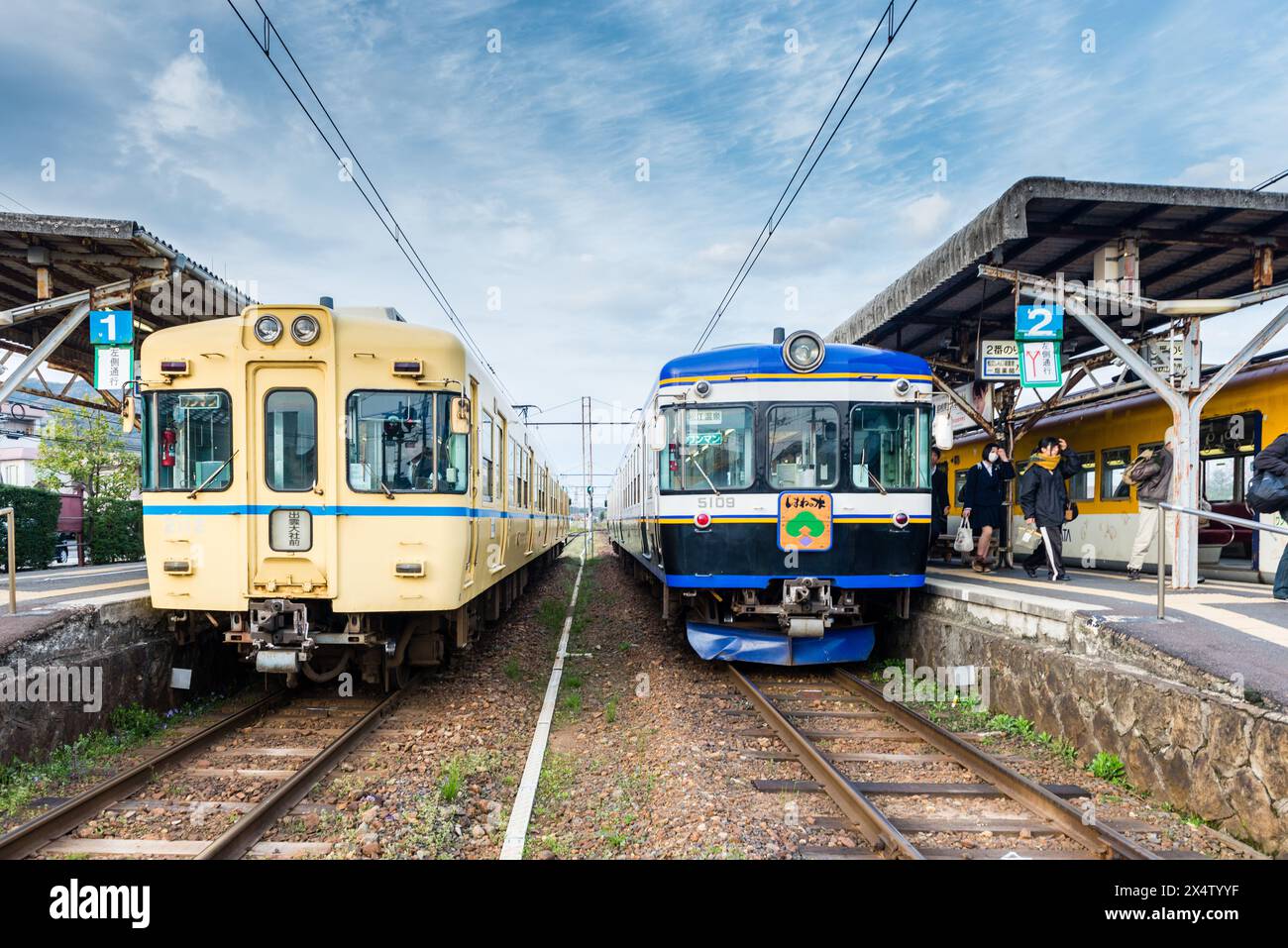Two trains are parked next to each other at a train station. The first train is yellow and the ...