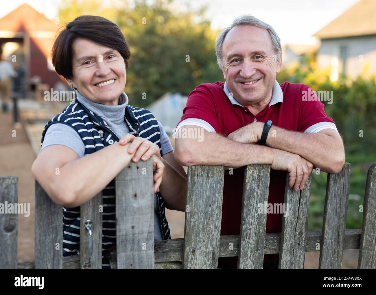 Portrait of a happy elderly couple in the garden near fence of their ...