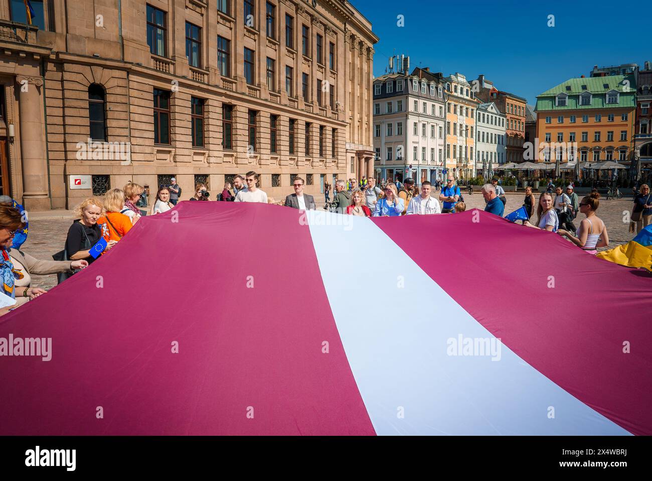 Vibrant Celebration in Old Town, Riga Large Latvian Flag Held High by Crowd Stock Photo - Alamy