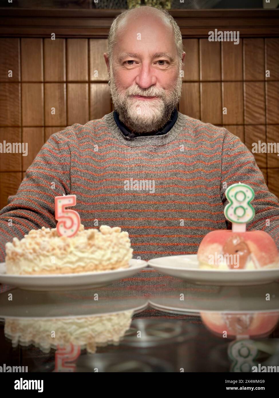 Smiling man sitting at a table with two birthday cakes with the numbers ...