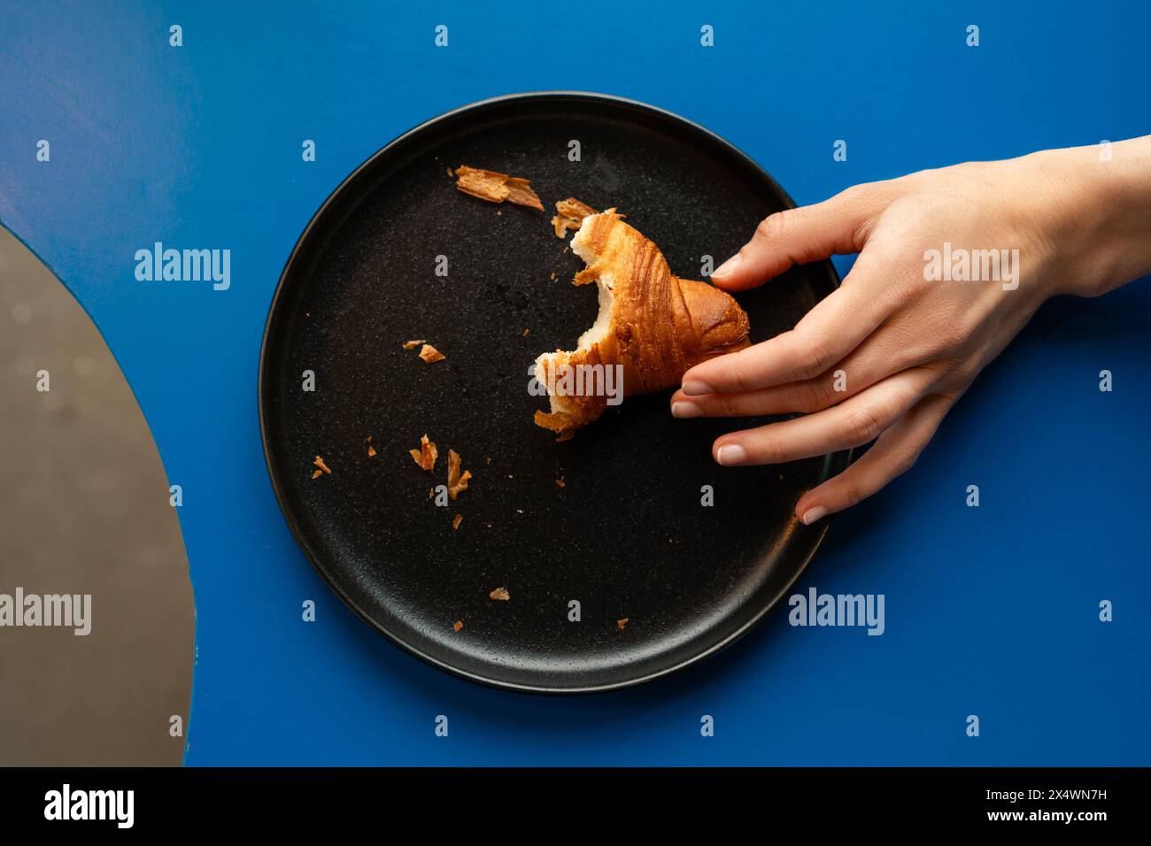 Overhead view of a Hand reaching for a half eaten croissant on a plate ...