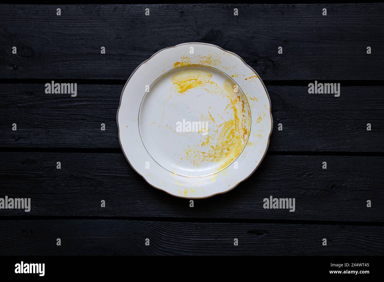 A white plate smeared with gold paint stands on a black board, dishes ...