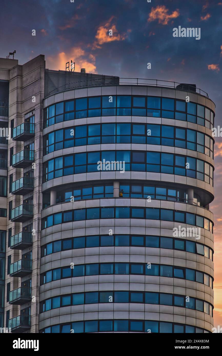 Modern glass building facade against a dramatic sunset sky, showcasing ...