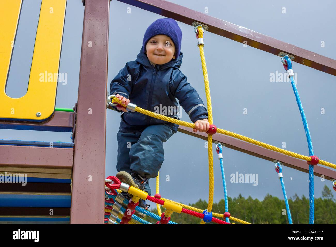 View from the ground on toddler boy walking over the rope bridge at ...