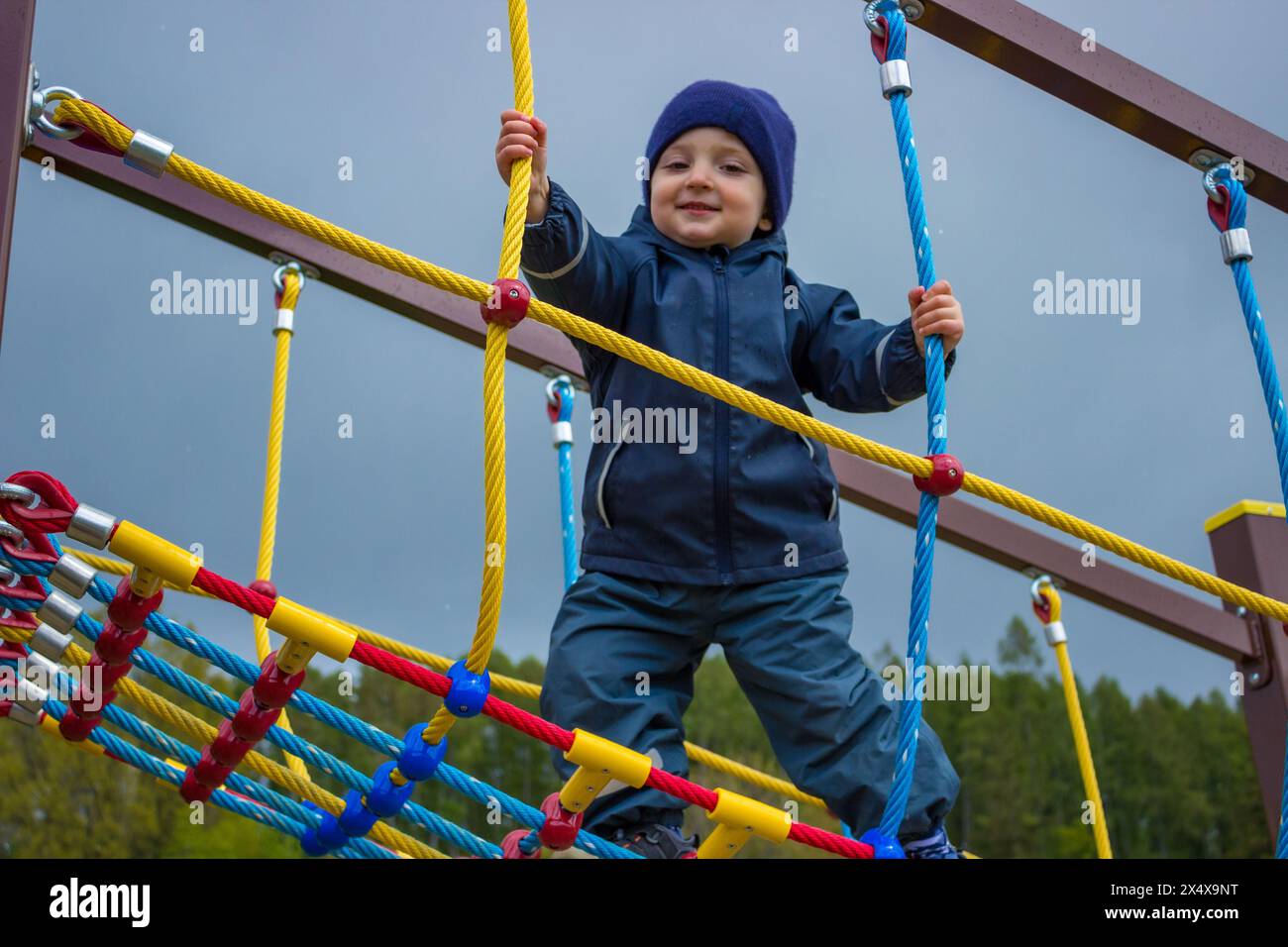 View from the ground on toddler boy walking over the rope bridge at ...