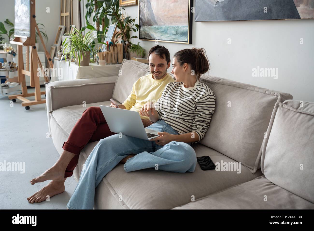 Happy relaxed creative couple of artist smiling sitting with laptop in ...