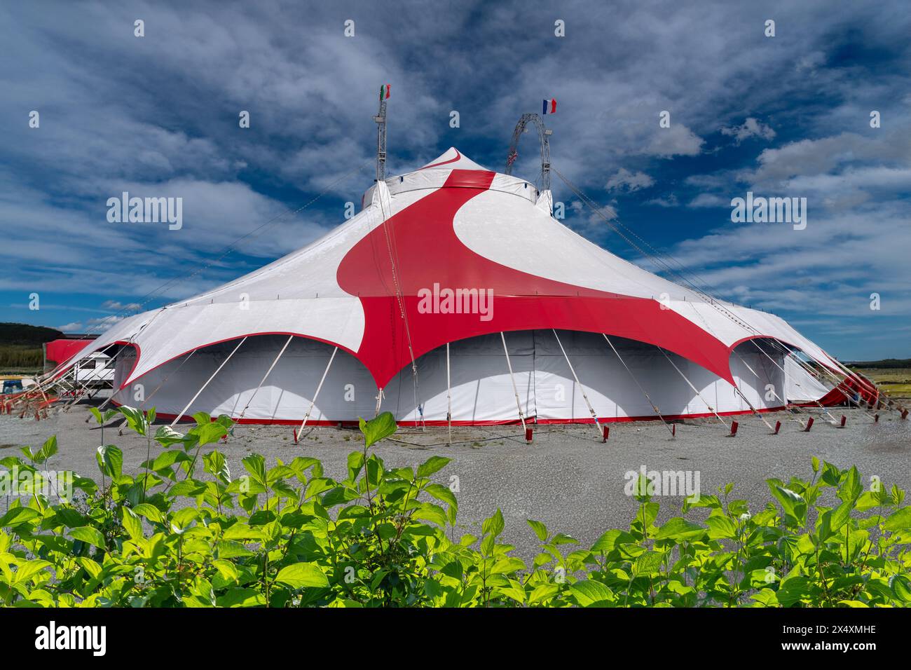 White circus marquee tent with red band on blue sky with white clouds ...