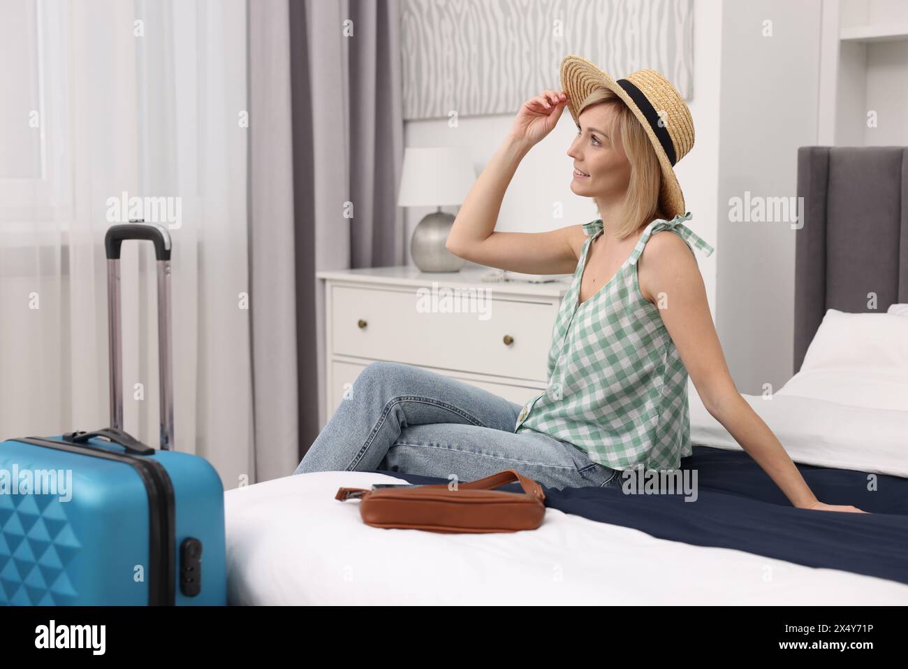 Smiling guest wearing hat relaxing on bed in stylish hotel room Stock ...