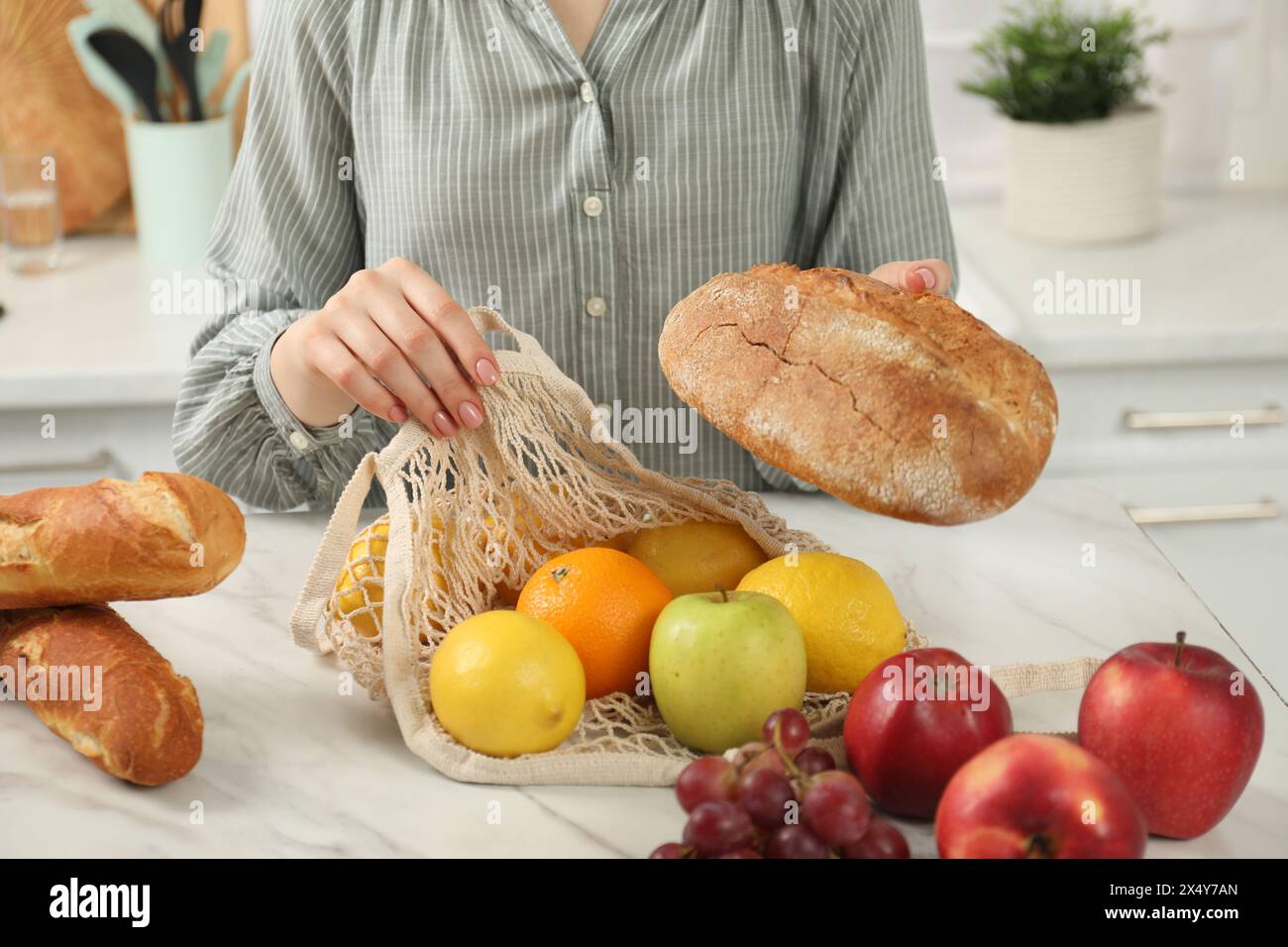 Woman with string bag of fresh fruits and bread at light marble table ...