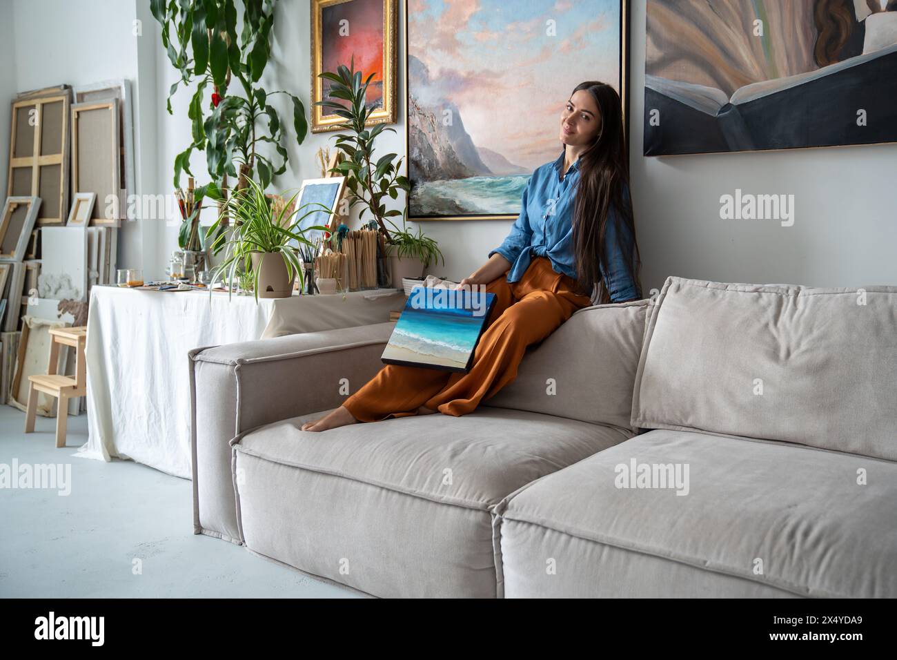 Creative satisfied female artist demonstrates picture, relaxed sitting ...