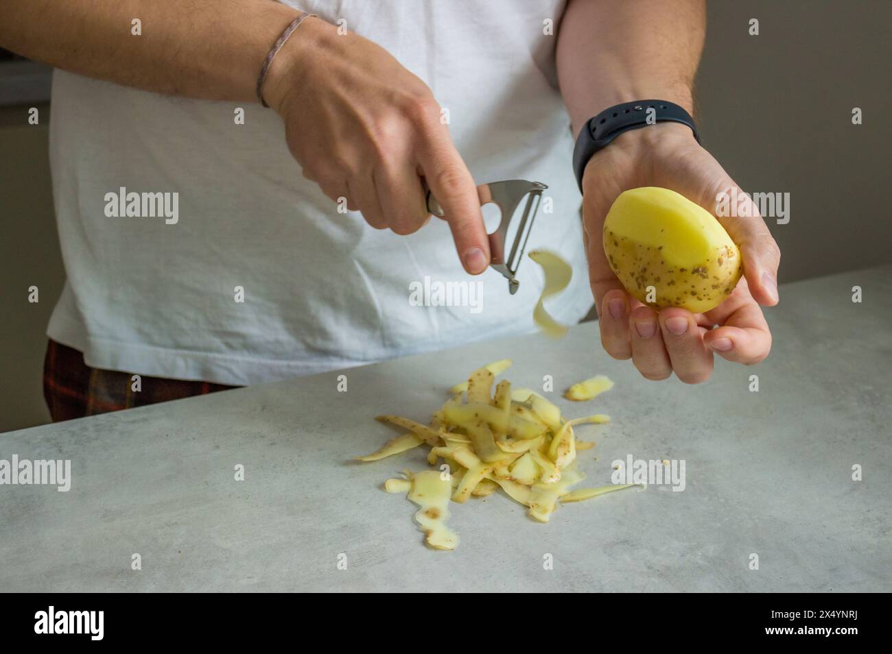 a man peeling potatoes on a grey kitchen counter with a potato peeler ...