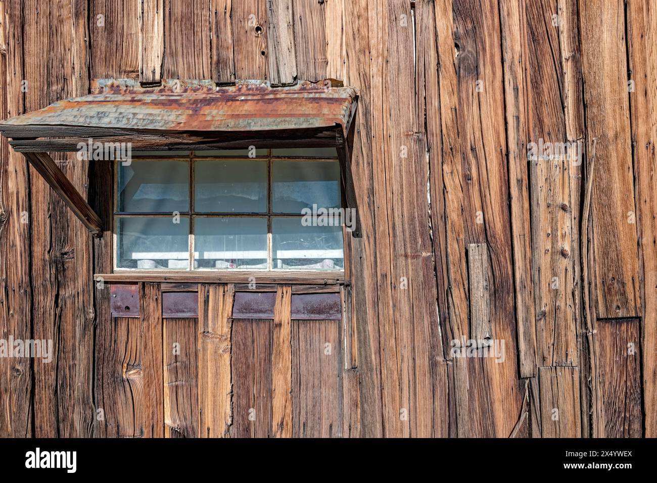 A window with a metal awning on the wall of an abandoned wooden shack ...