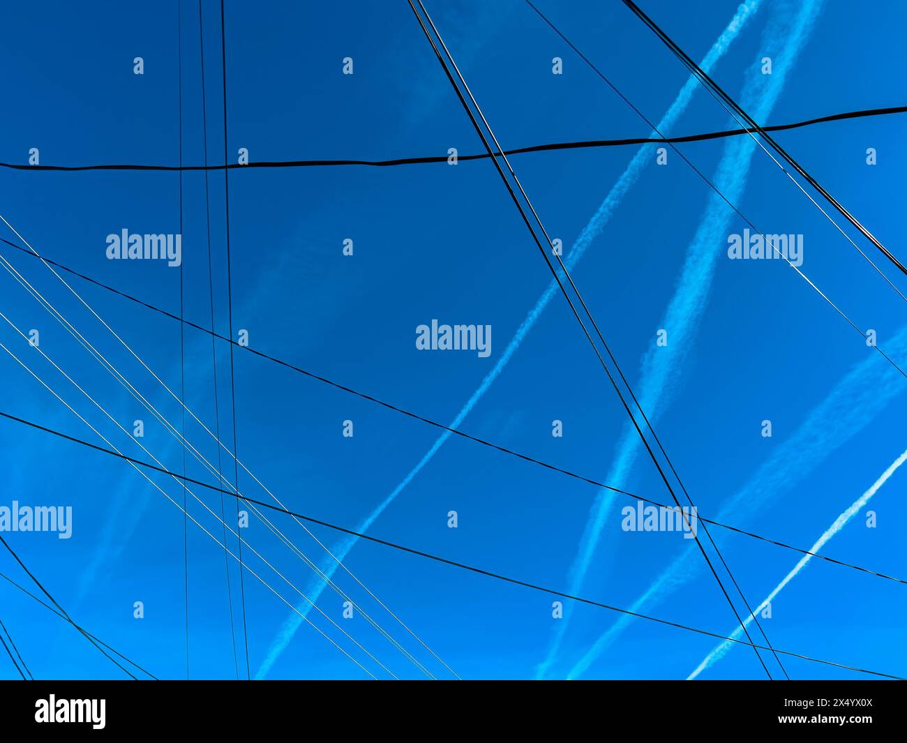 Pattern of airplane contrails and electrical wires over blue sky in ...