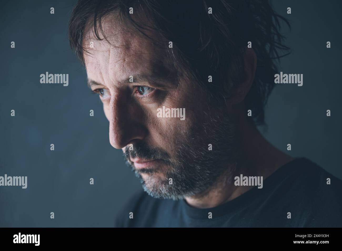 Low key portrait of adult unkempt man in his 40s, looking out the ...