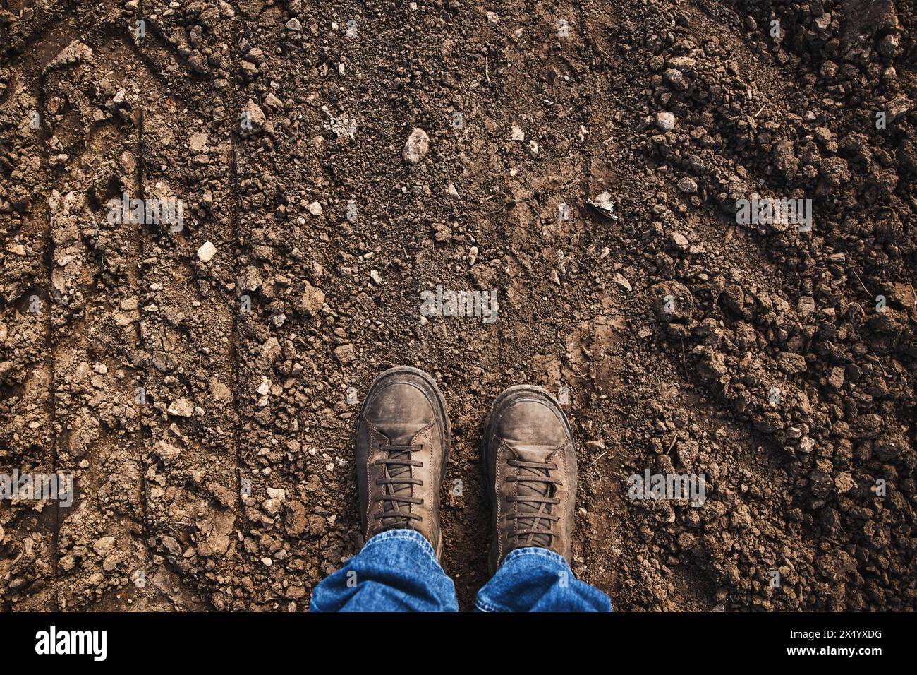 Top view of farmer's feet in boots standing on countryside dirt road ...