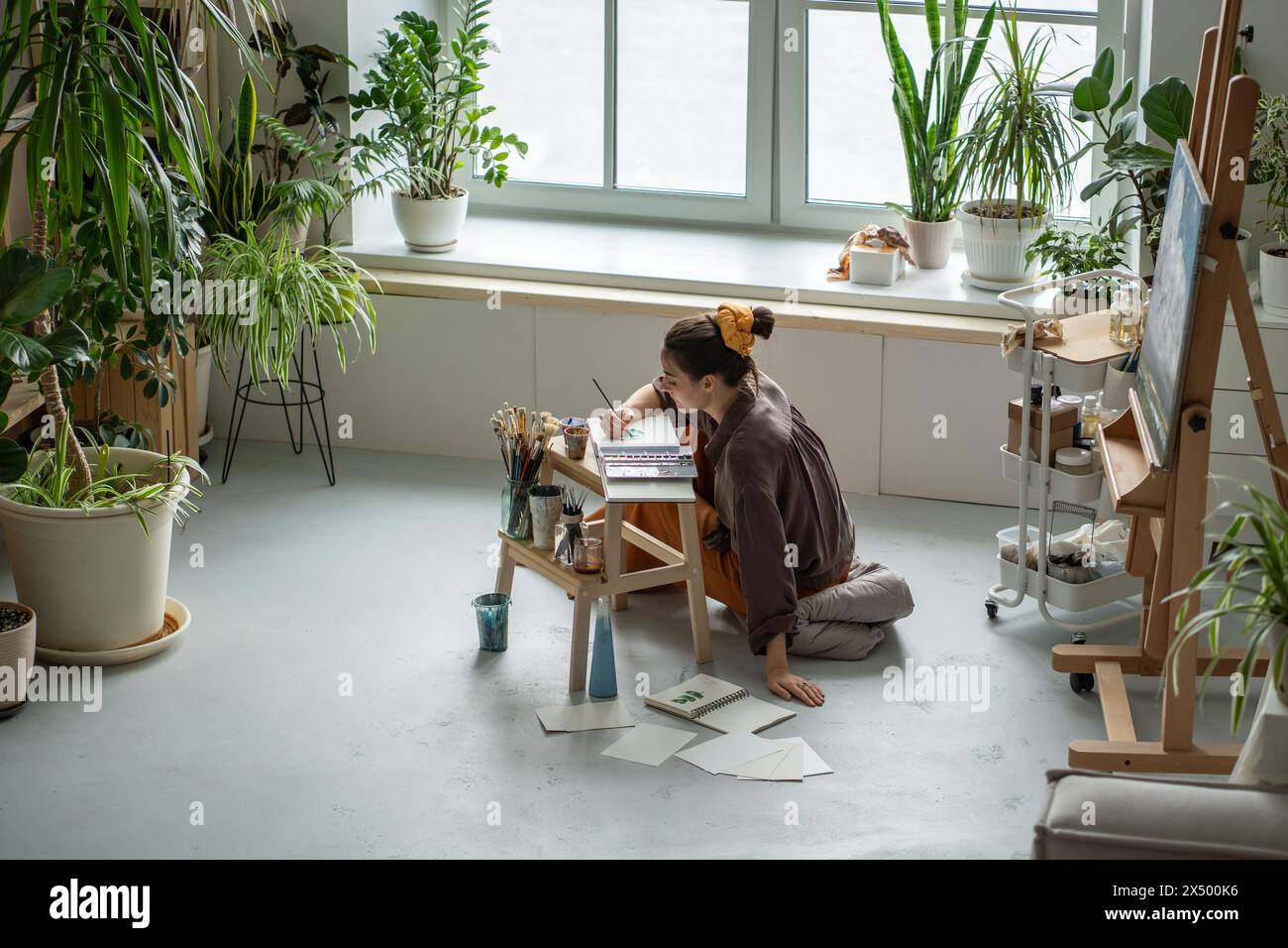 Focused woman artist sit comfortably on floor inspirationally painting ...
