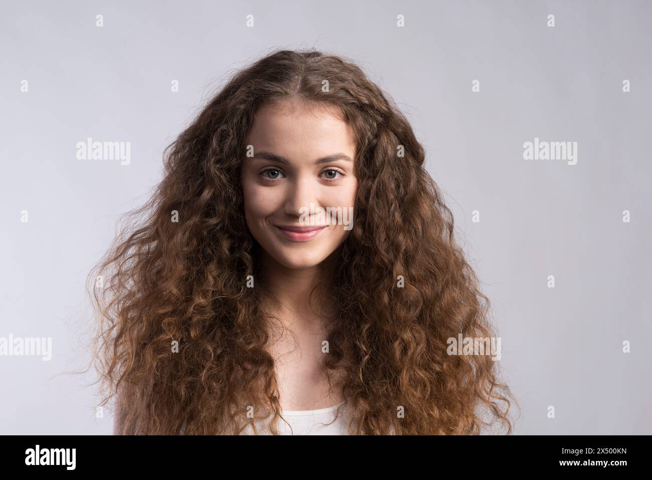 Portrait of a gorgeous teenage girl with curly hair. Studio shot, white ...