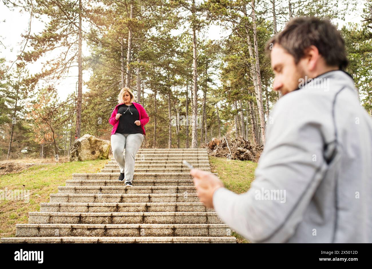 Overweight woman running down the stairs, personal trainer checking her ...