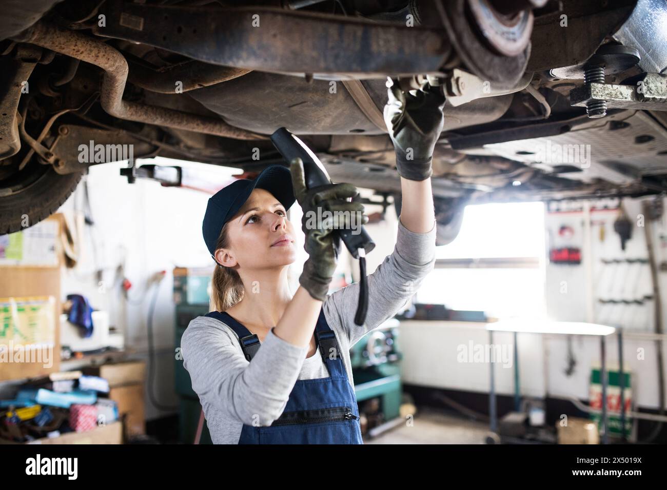 Female auto mechanic elevating car on car lift, working underneath ...