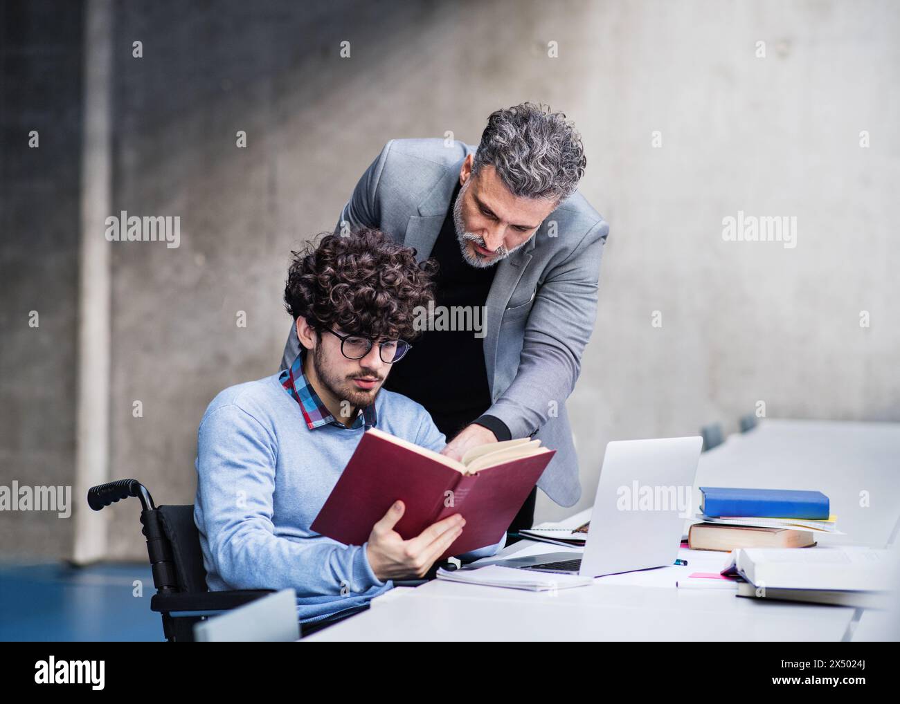 Handsome university professor helping student in wheelchair, showing ...
