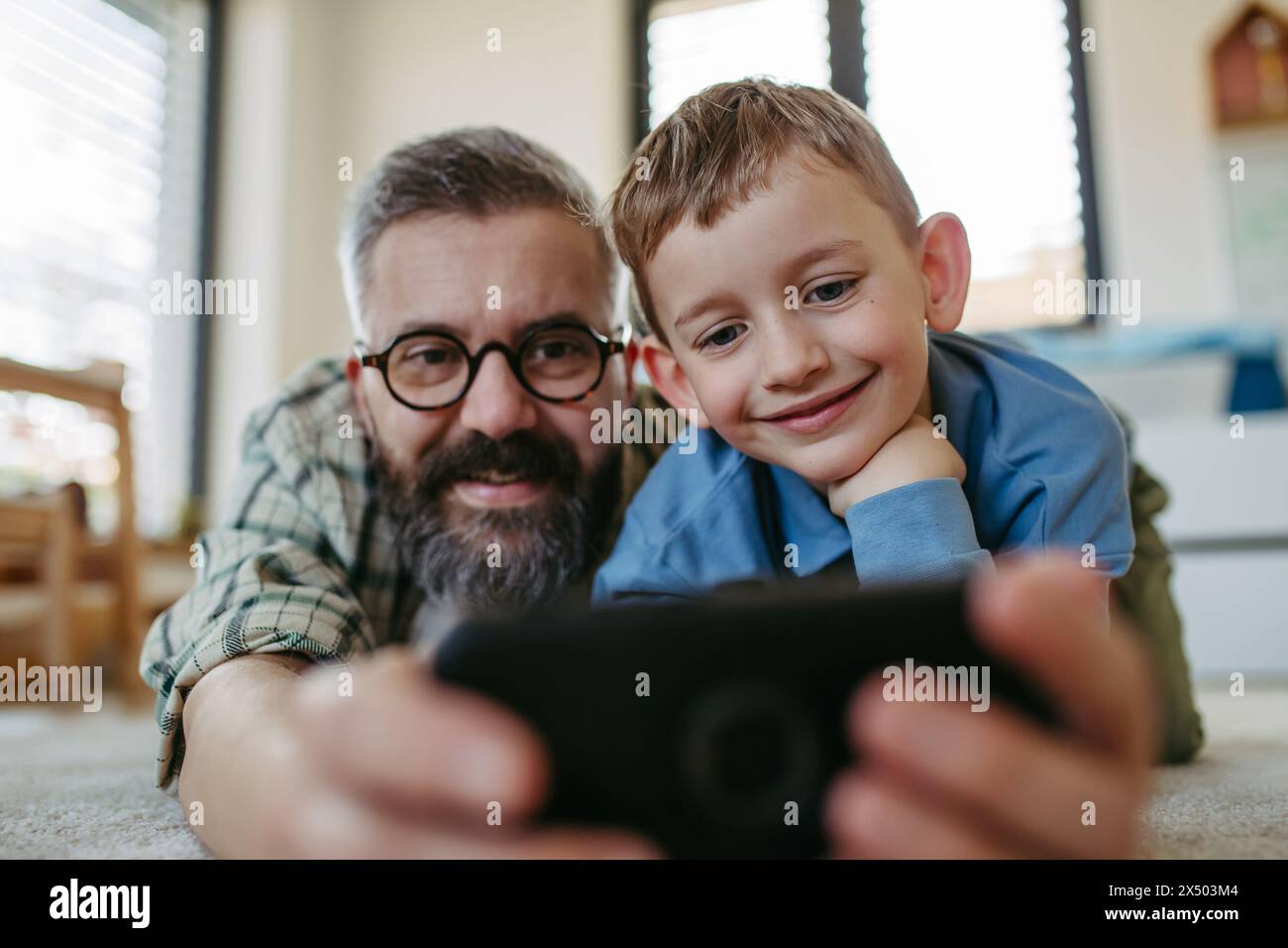 Little boy making selfie on smartphone with father, lying on floor in ...