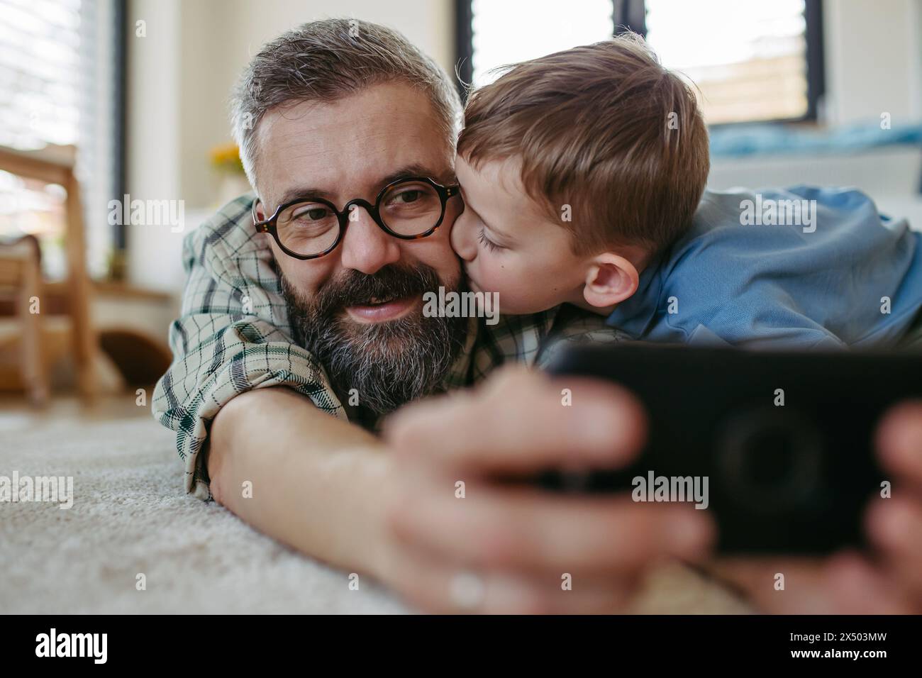 Little boy making selfie on smartphone with father, lying on floor in ...
