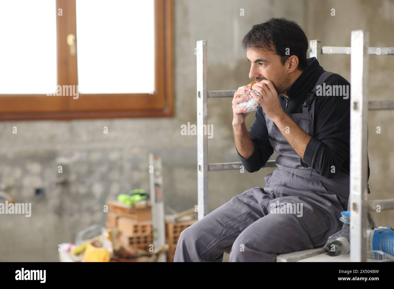 Construction worker eating sandwich at breakfast sitting on scaffold ...