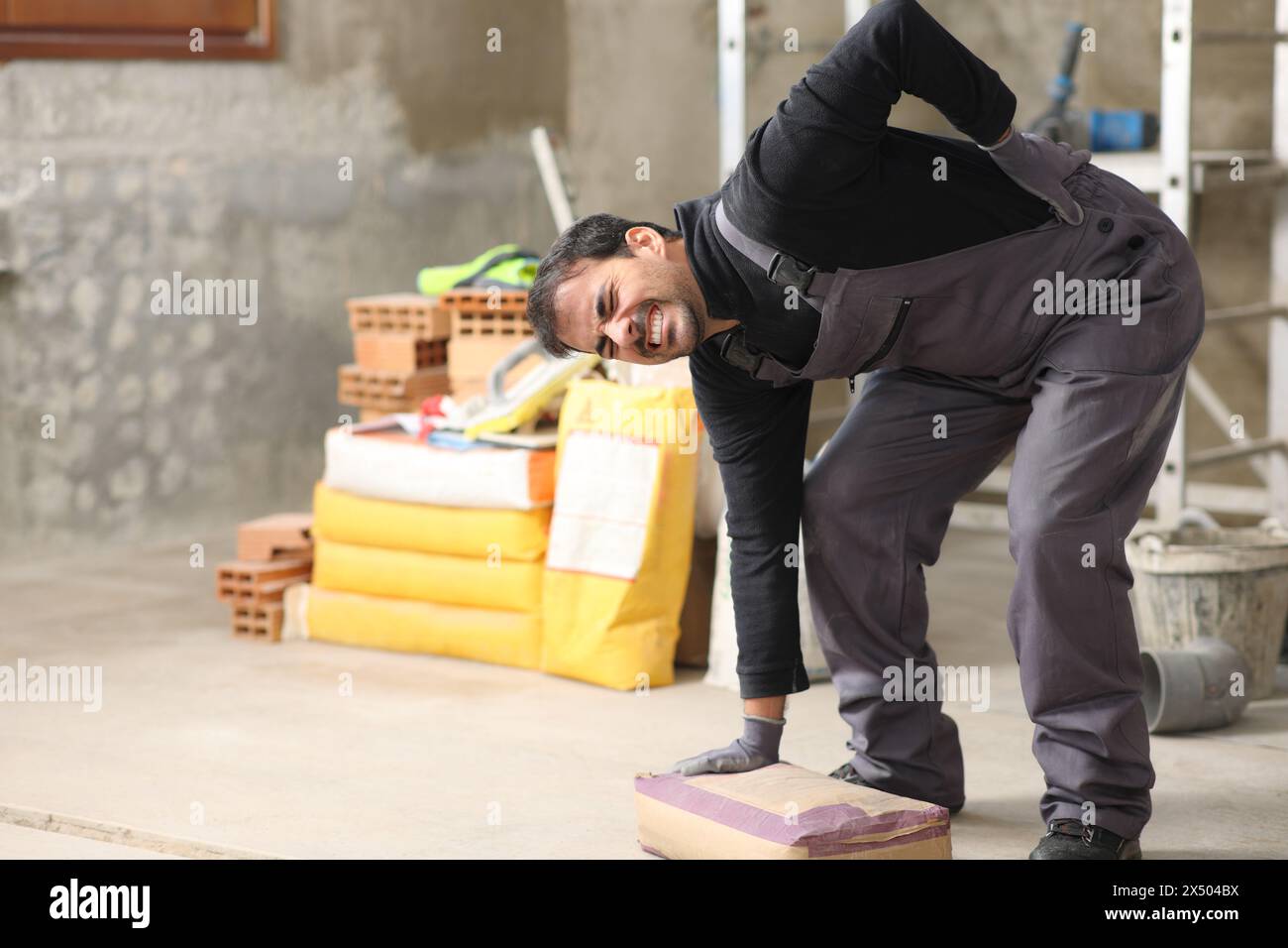 Construction worker suffering back ache lifting a weight in a house ...