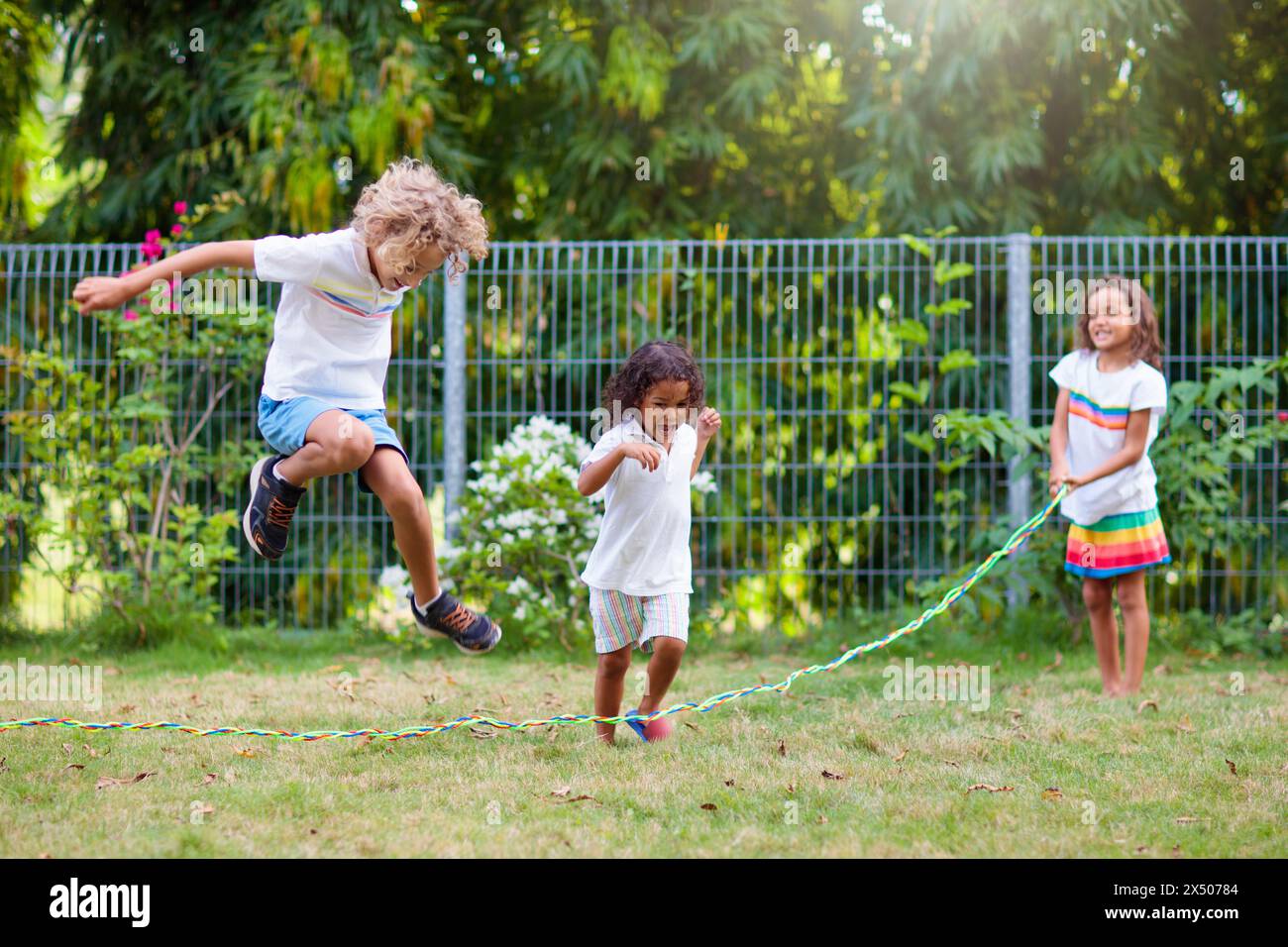 Happy kids play outdoor. Children skipping rope in sunny garden. Summer holiday fun. Group of ...