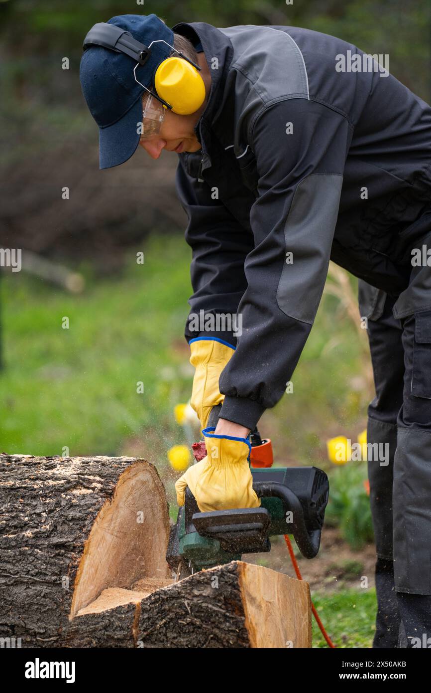 A man in uniform cuts an old tree in the yard with an electric saw ...