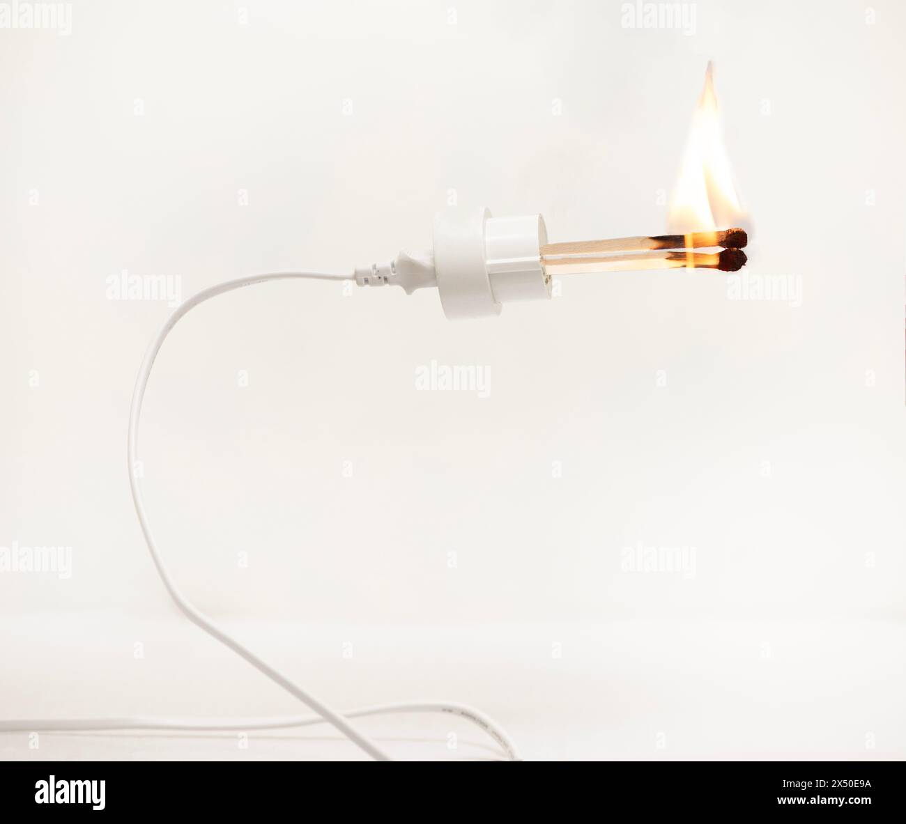 Conceptual electric cable and plug on fire against a white background ...