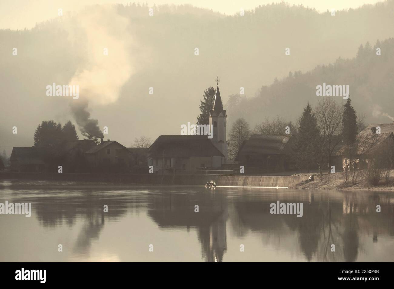 Cold morning scene on a lake shore with smoke coming up from a chimney ...