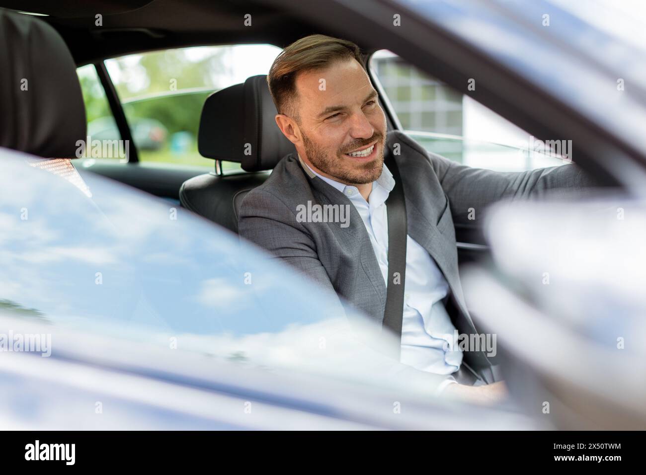 Joyful driver smiles while holding the wheel, cruising down the road in ...